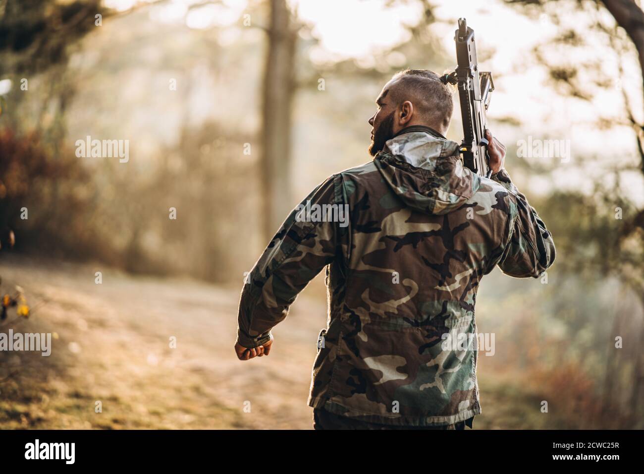 A camouflage soldier playing airsoft outdoors in the forest, sunset ...