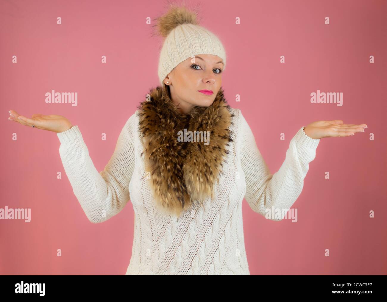 Portrait of a doubtful woman dressed in winter clothes standing isolated over pink background ...