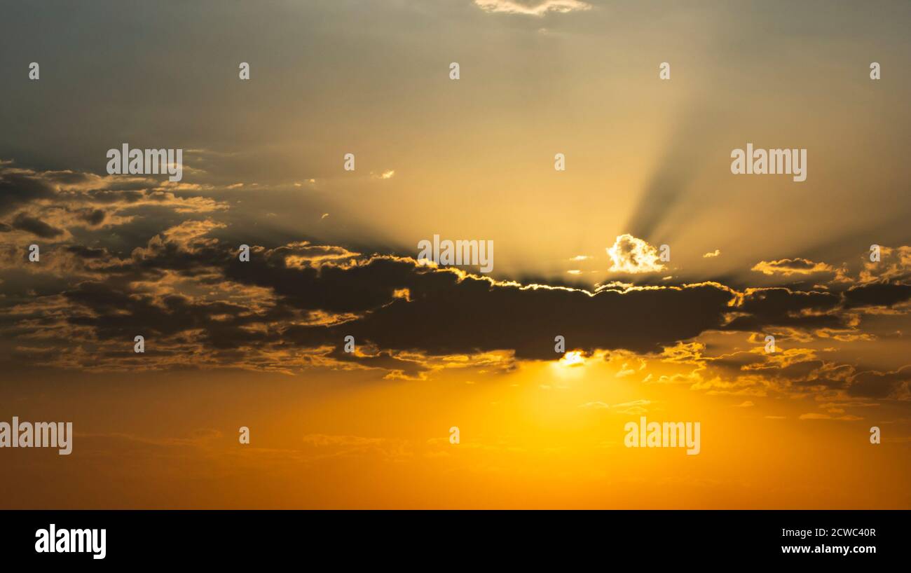 The sun hides behind a layer of clouds at sunrise, only its rays coming ...