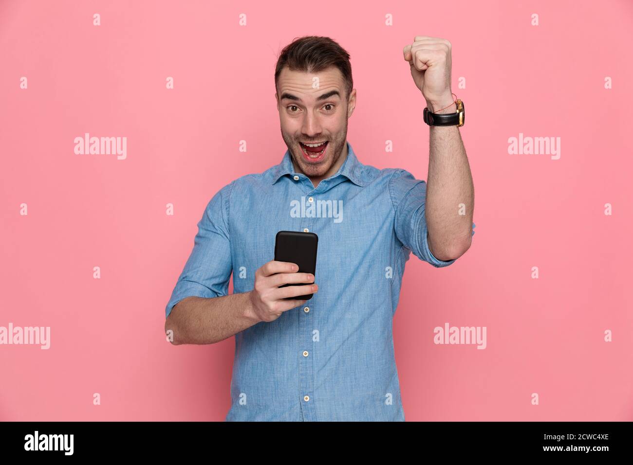 happy casual man raising his fist, texting on his phone and wearing a ...