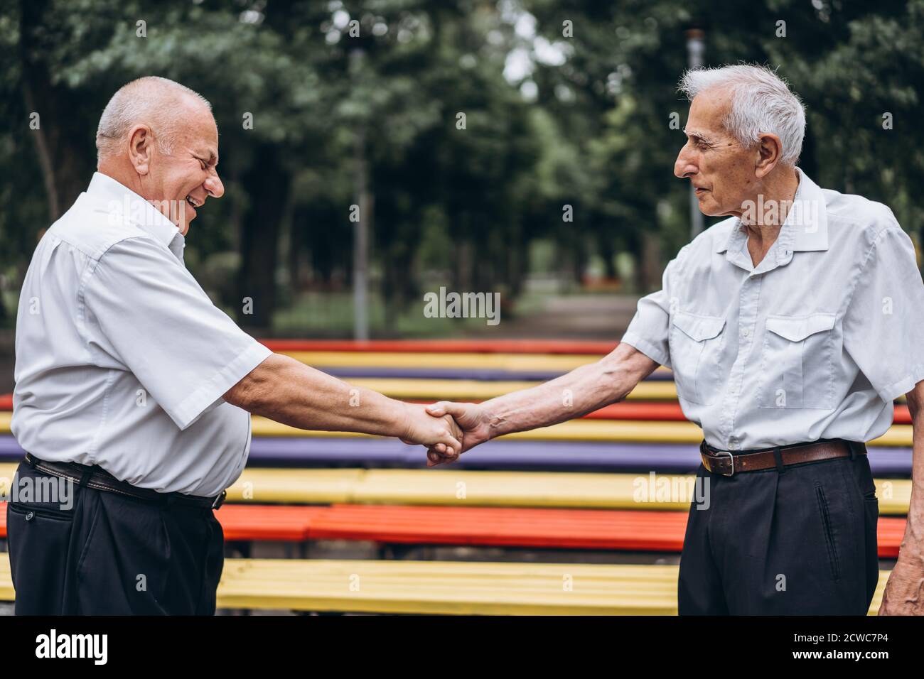 Two old senior adult men have a conversation outdoors in the city park ...