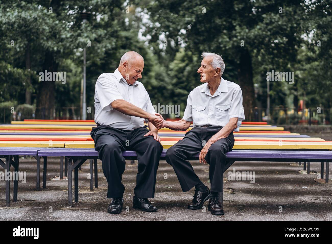 Two old senior adult men have a conversation outdoors in the city park ...