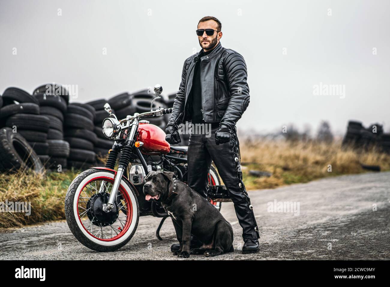 Biker in a leather suit and his dog stand near a red motorcycle on the ...