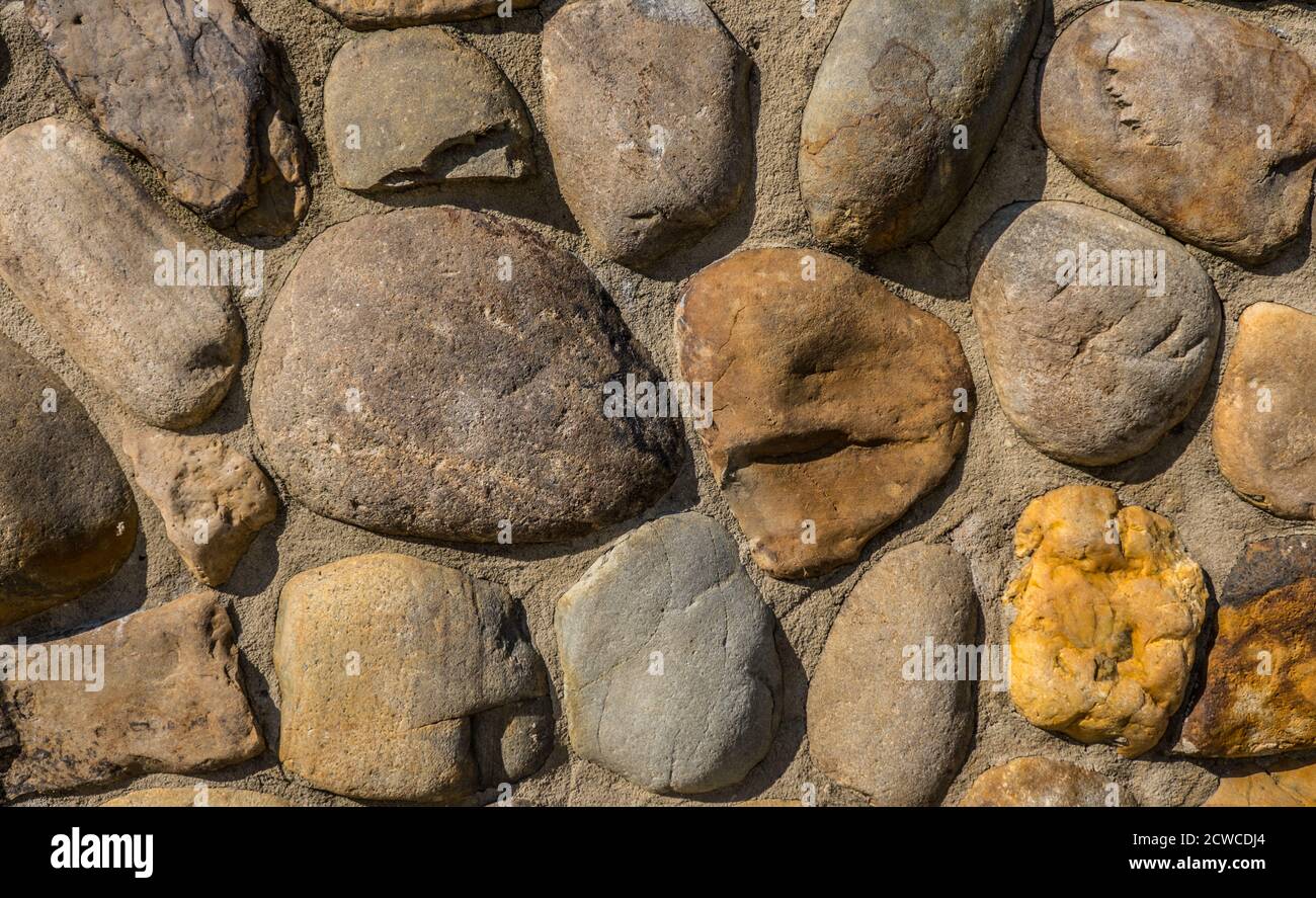 A wall of rocks and stone of different sizes shapes and color set in ...