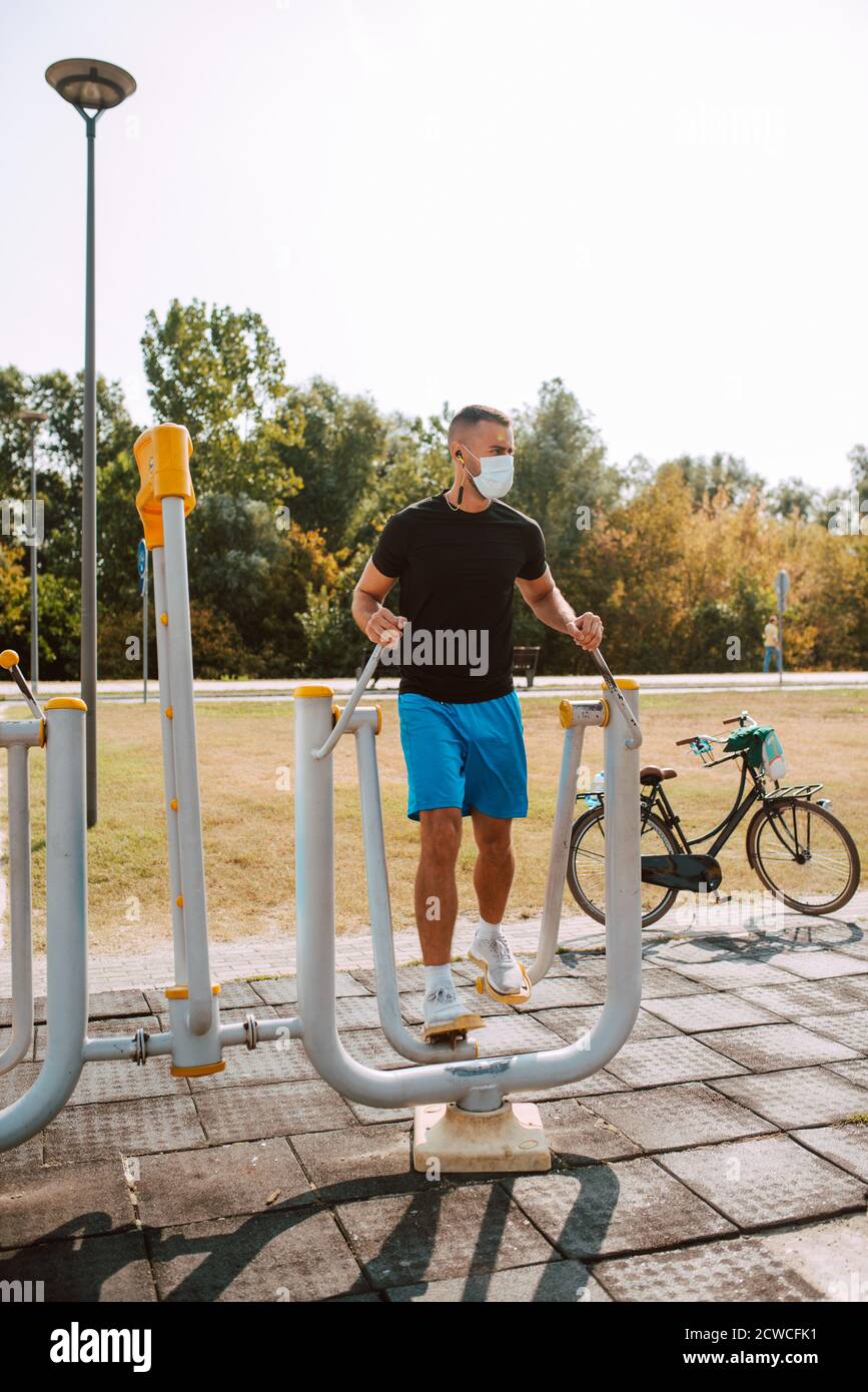 Fit young male caucasian athlete with face mask trains on arm and leg ...