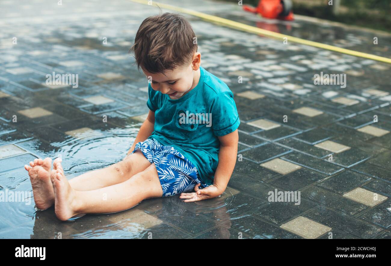 Wet caucasian boy playing in the yard with water sitting on the ground ...