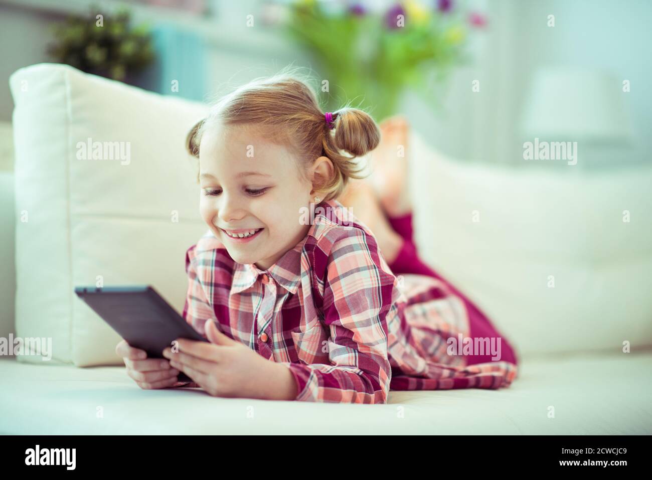 Portrait of cute little child girl laying on sofa with tablet at ...