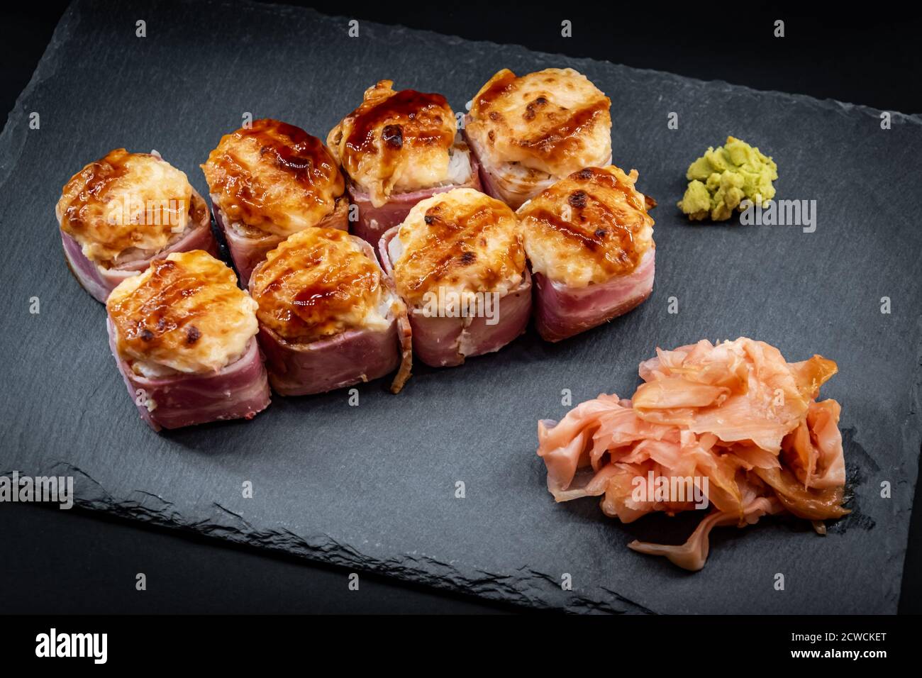 Served warm sushi rolled in bacon with ginger and wasabi on a black ...