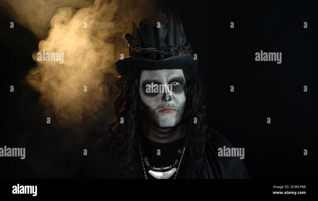Creepy long hair man with skeleton makeup in top-hat with feathers. Guy ...
