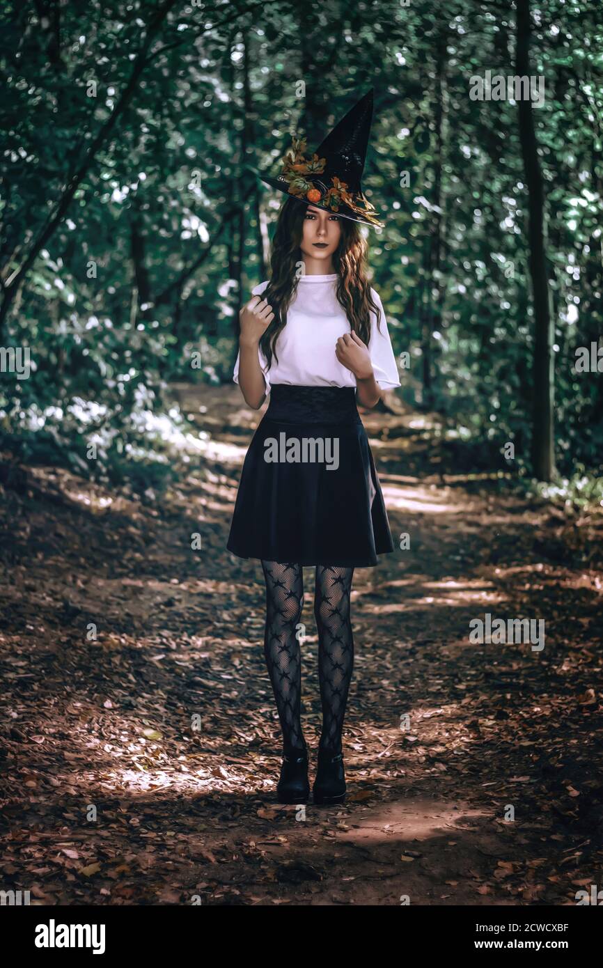 Young pretty witch in black hat close up in the forest. Whitch ...