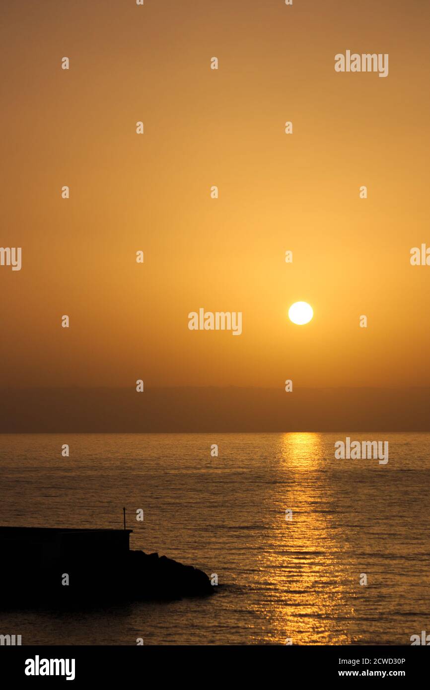 Vertical image of a sunrise near a sea port in which the orange colors ...