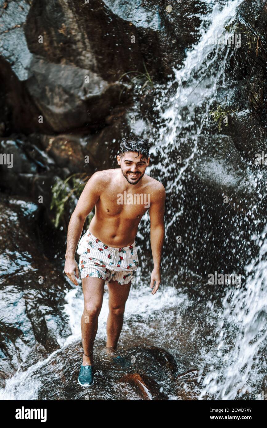 Young Caucasian athletic male at a waterfall near rocks enjoying the ...