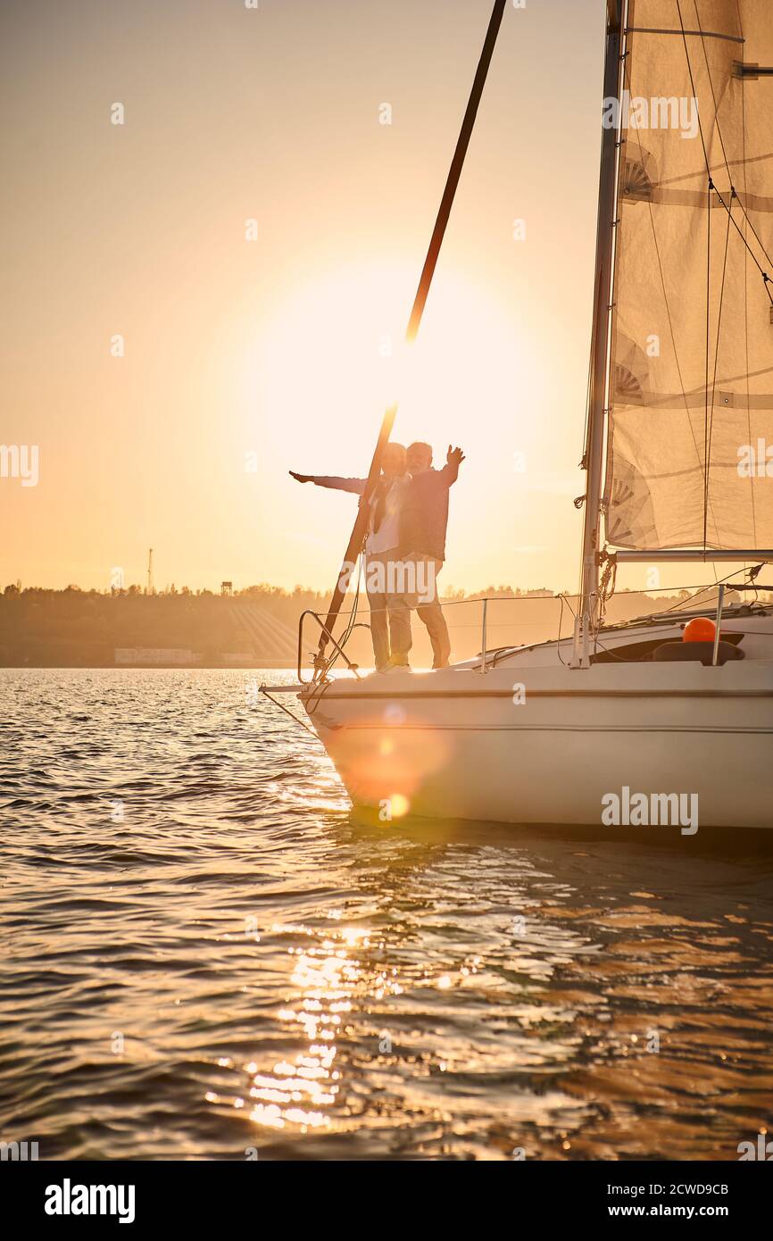 Romantic senior couple enjoying sailing together at sunset, stretching ...