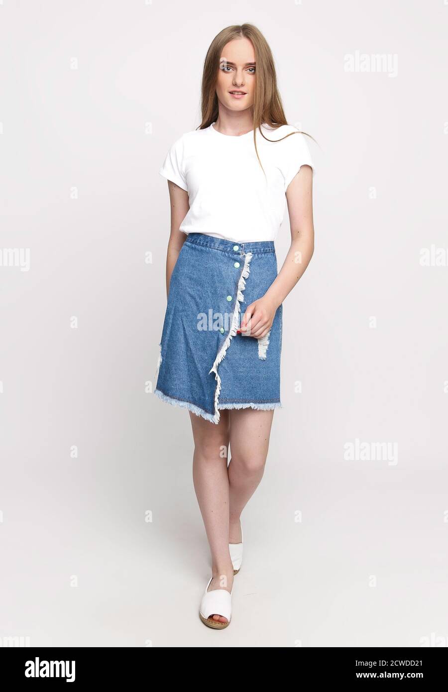 cute young slender woman in a white t-shirt and denim fashionable skirt ...