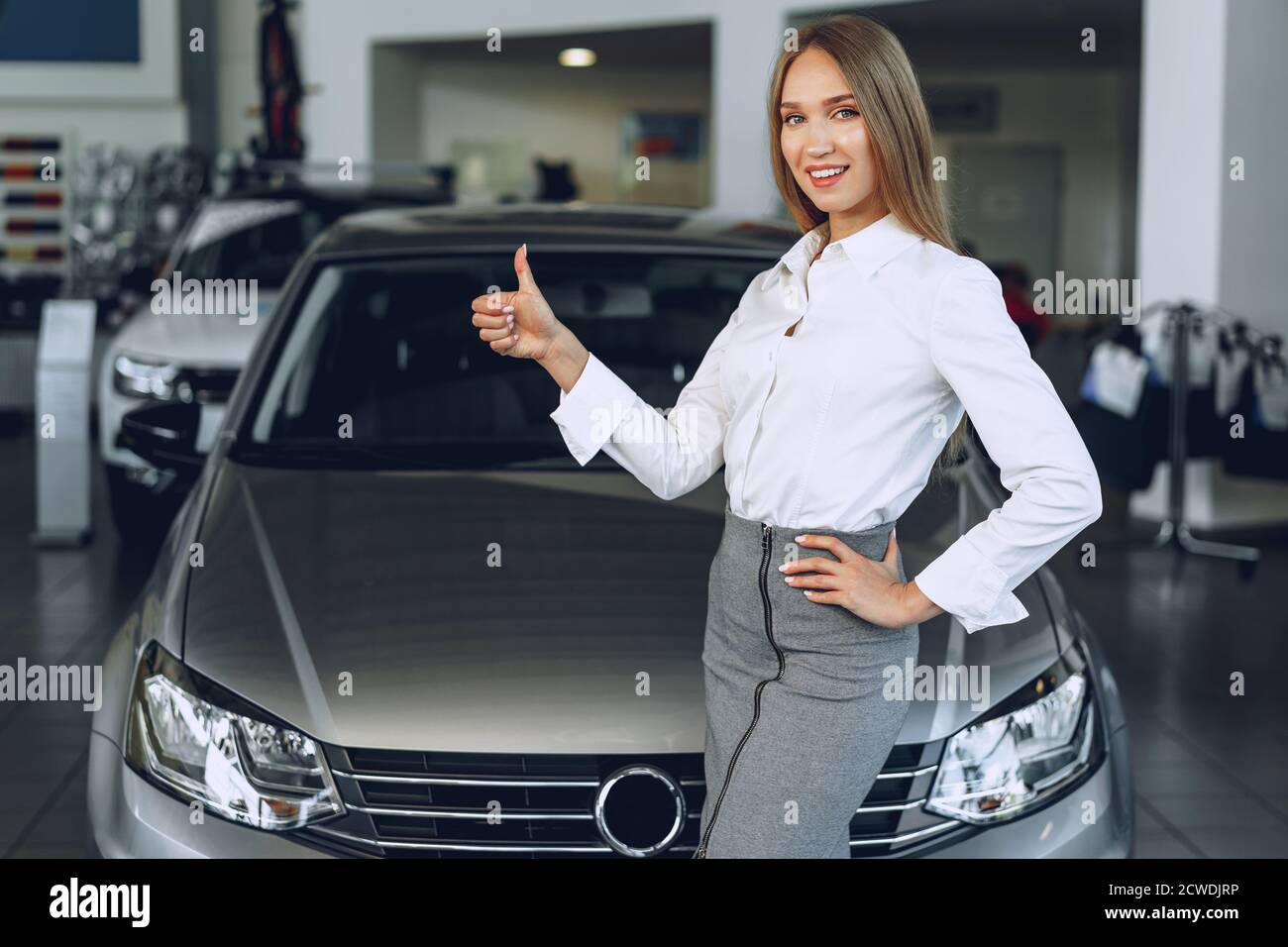 Happy beautiful young woman car dealer in showroom Stock Photo - Alamy