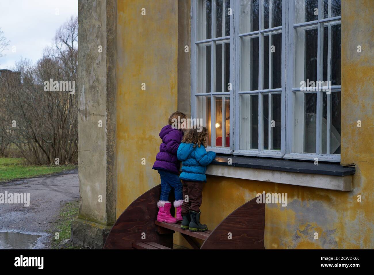 Two children standing on stairs to peer through a window Stock Photo ...