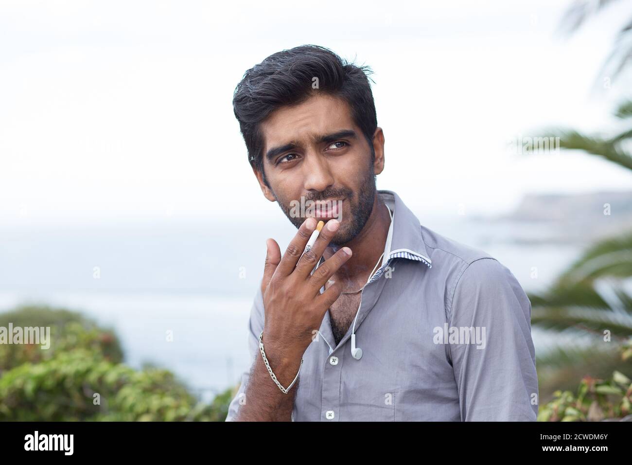Happy ethnic man smoking cigarette, smiling, thinking looking sidewards ...