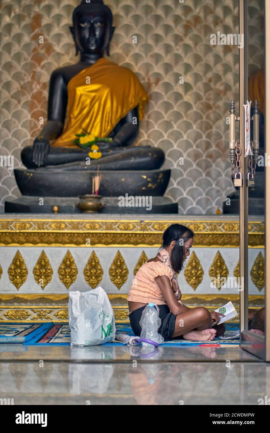 Woman Buddhist reading scripture beneath a Buddha statue. Thailand ...