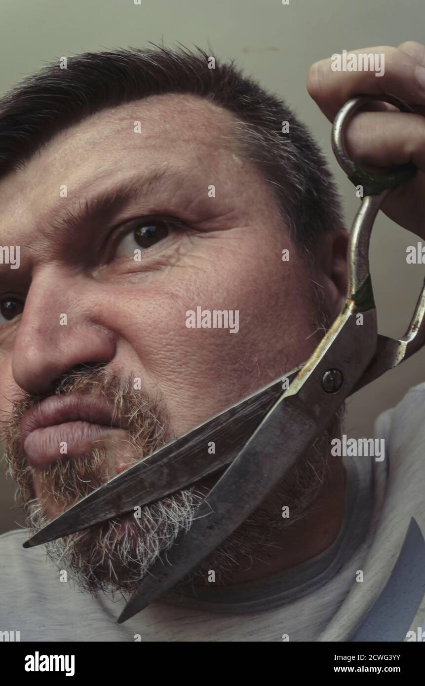An adult man cuts his own beard with old huge scissors. Unusual ...