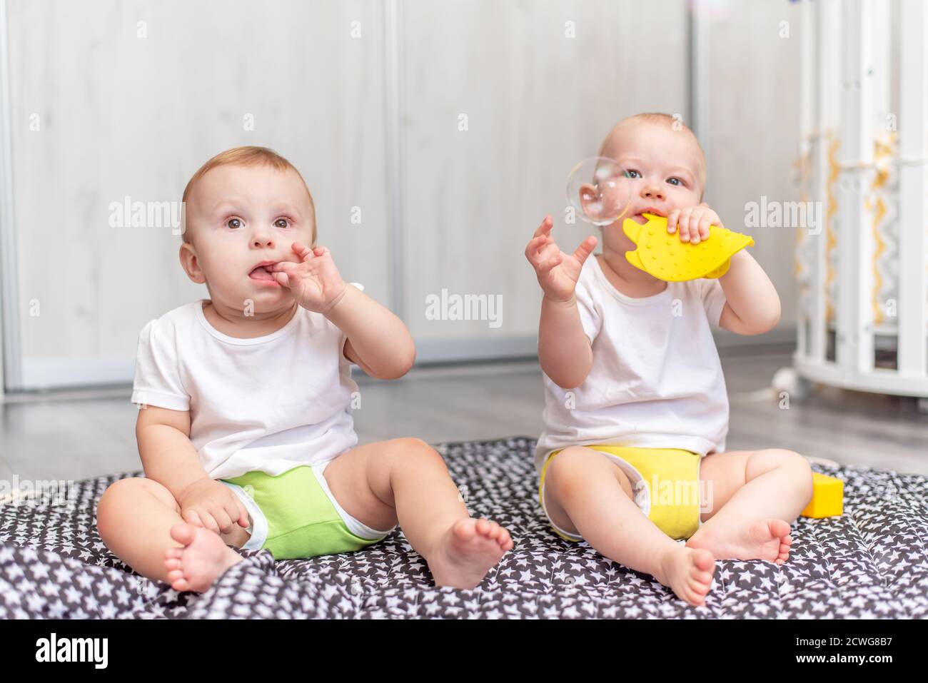 Cute happy babies play together on the floor with toys and take them in ...