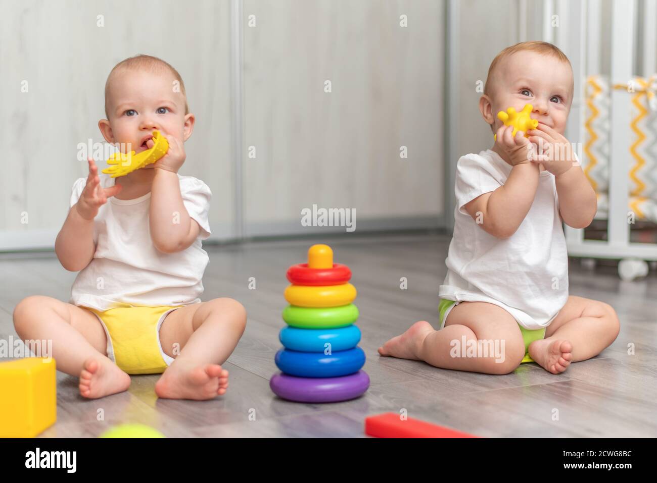 Cute happy babies play together on the floor with toys and take them in ...