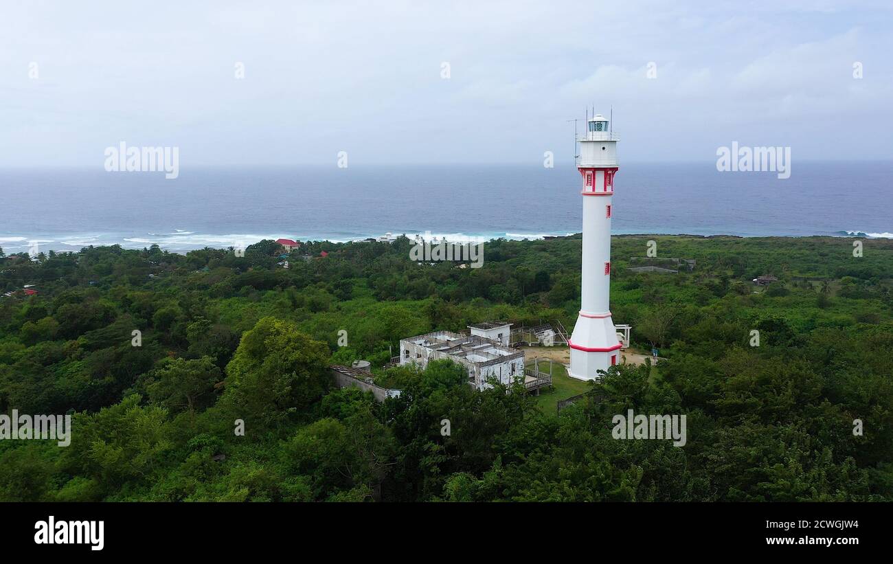 White tower lighthouse on a large island, top view. Rainforest hill and ...