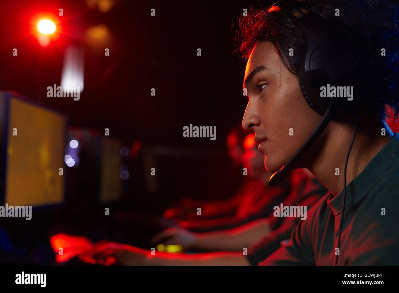 Side view of young gamer wearing headphones playing computer games with ...