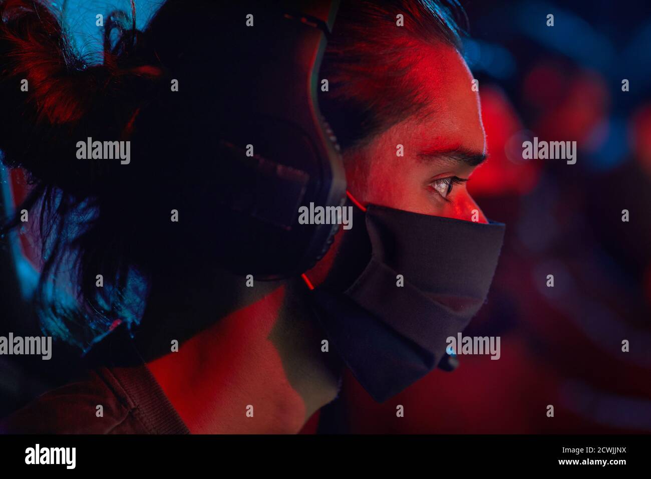 Side view of young hacker in headphones and in protective mask using ...