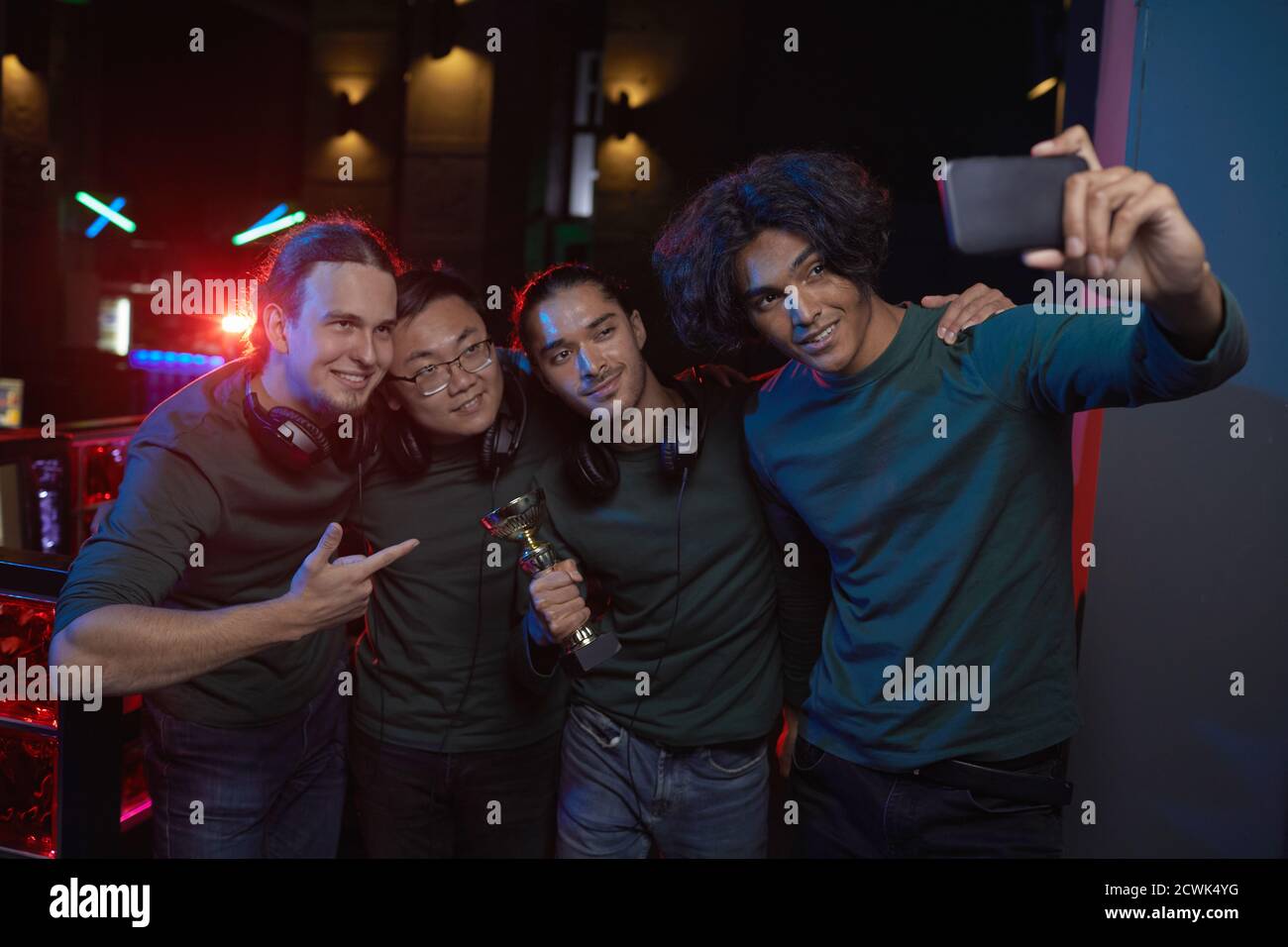 Group of gamers posing at camera of mobile phone with trophy after ...
