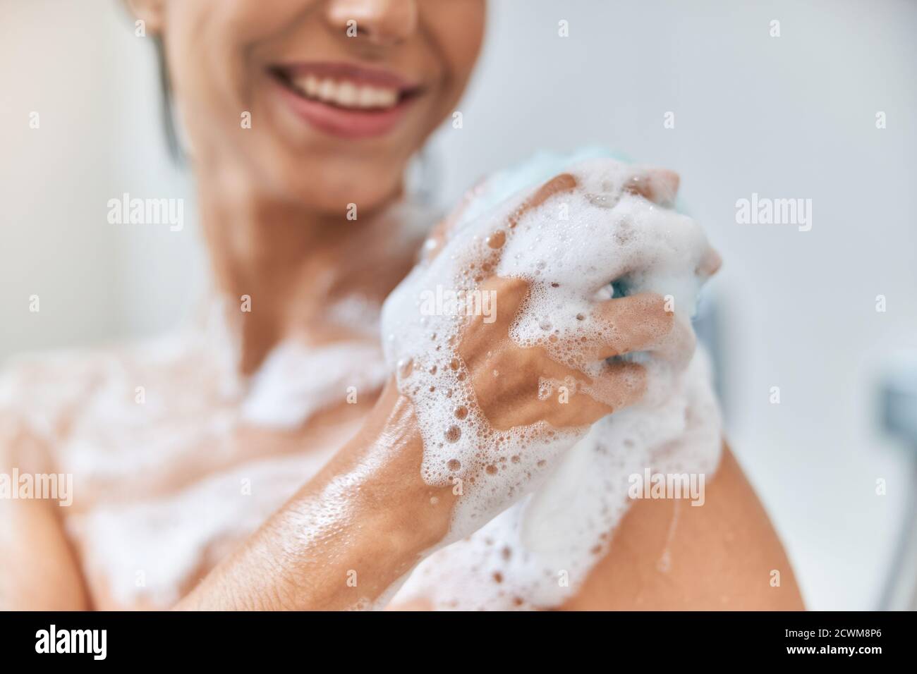 Cheerful young woman washing her body with bath loofah Stock Photo - Alamy