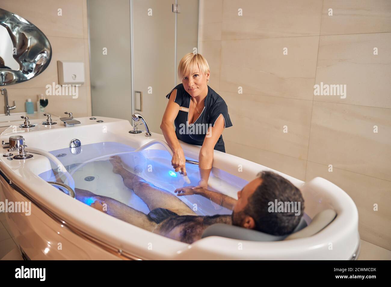 Beautiful young woman performing hydromassage procedure in spa salon ...