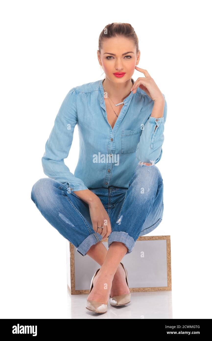 attractive woman pose in studio seated with hand on knee touching face ...