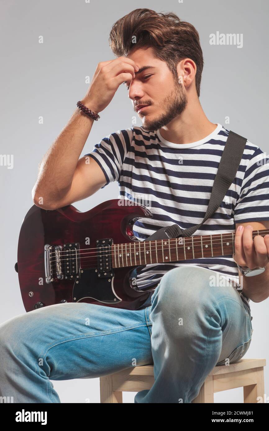 young guitarist playing his instrument seated on chair while thinking ...