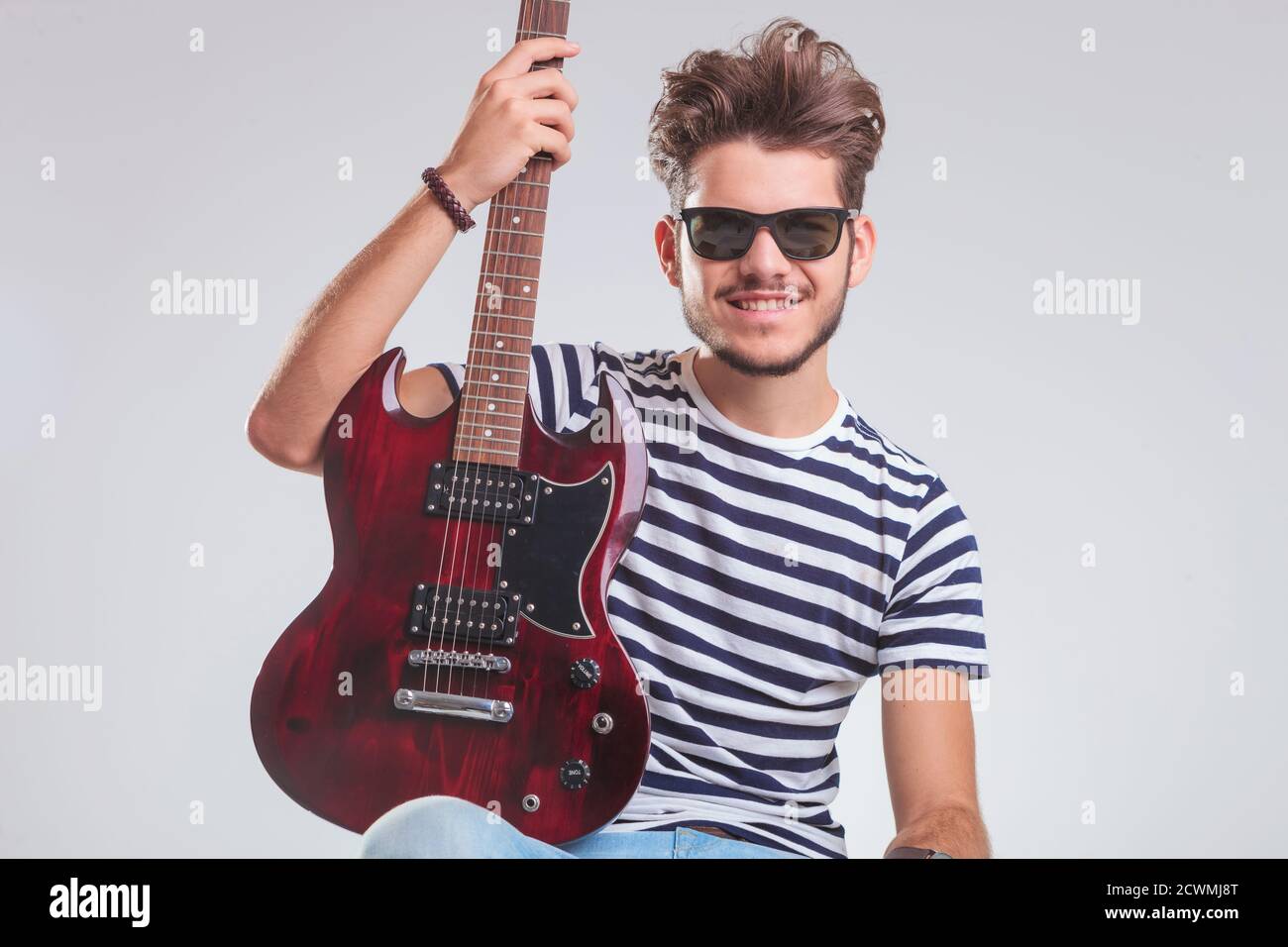 young rocker posing in studio background with electric guitar in his ...