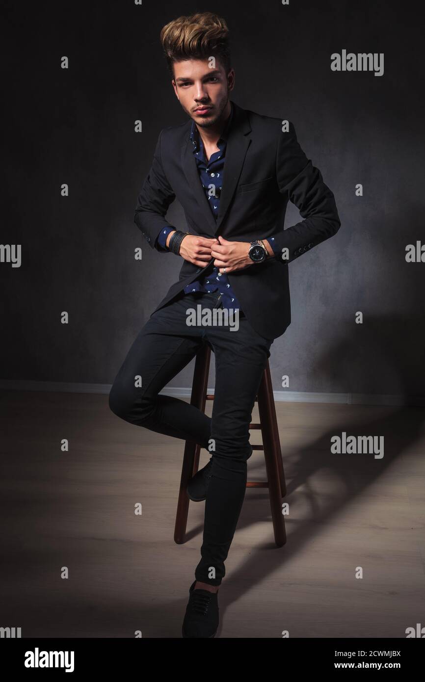 portrait of attractive elegant guy posing seated in dark studio ...