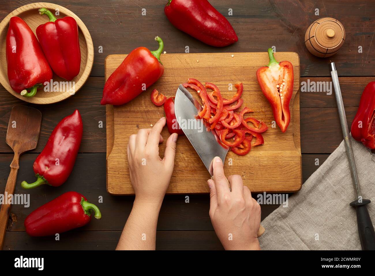 woman cuts red bell pepper into pieces on wooden board, brown wooden ...