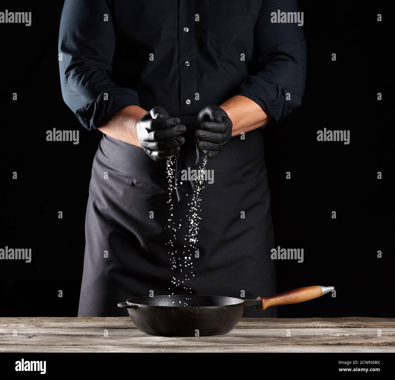 white coarse salt is poured from the chef's palms, black background, a ...