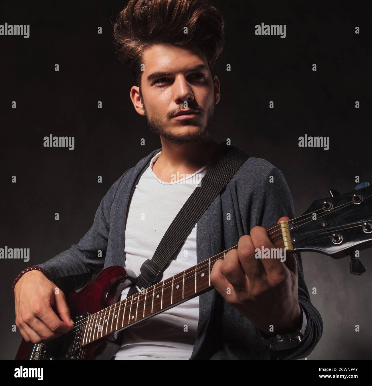 young cool indie artist playing guitar in studio background while ...