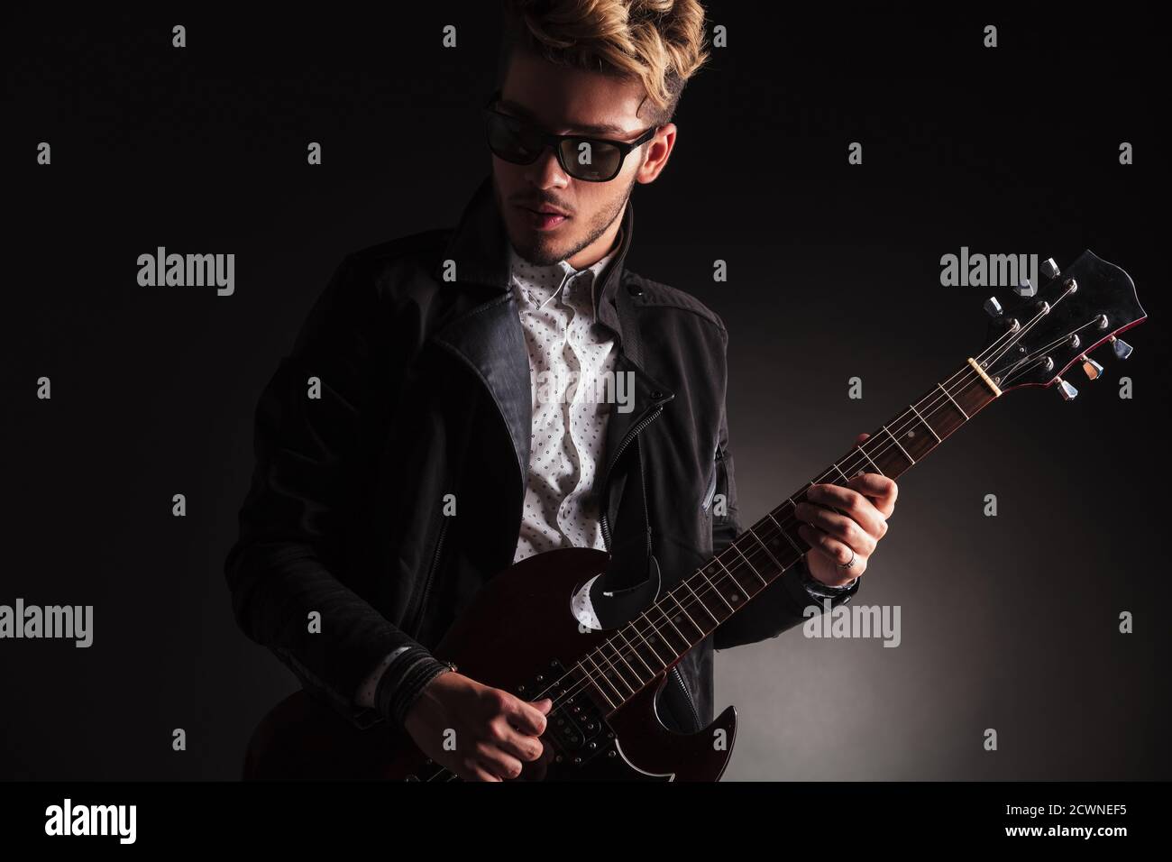 cool young guitarist playing his electric guitar on black studio ...