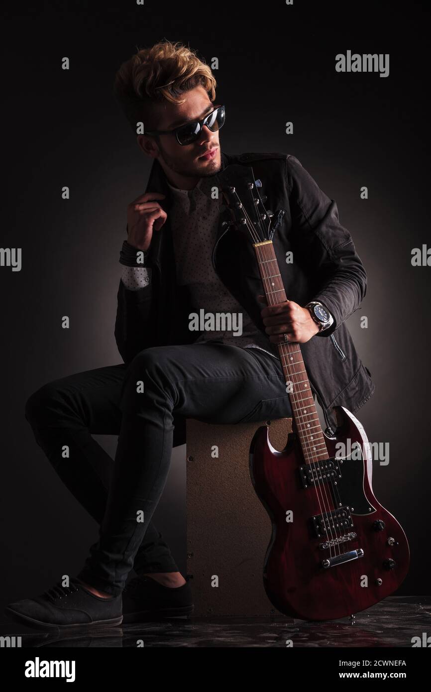 side view of a young guitarist sitting and looking back while he holds ...