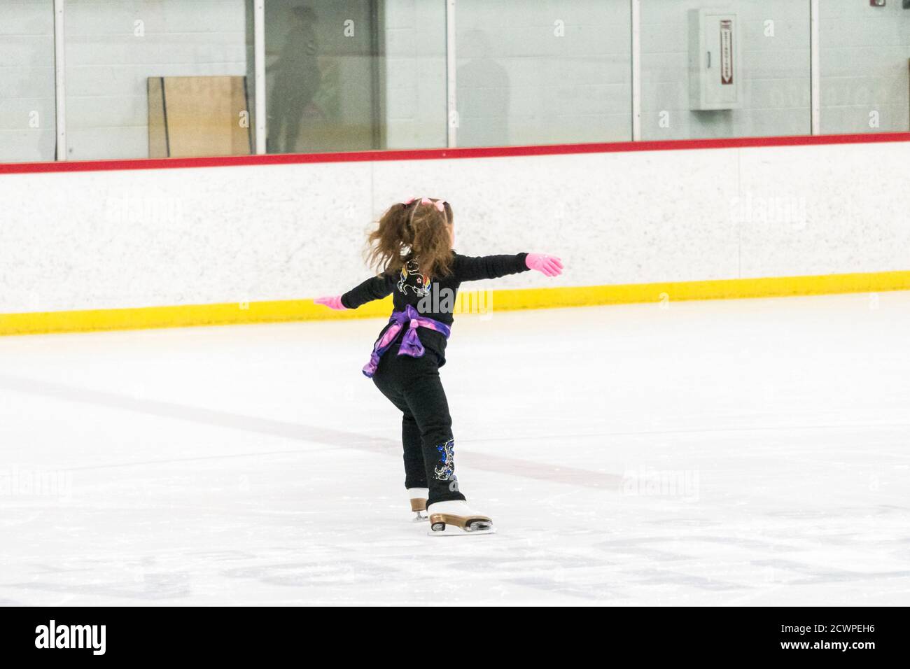 Little girl practicing figure skating moves on the indoor ice rink ...