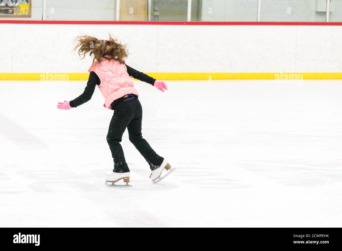 Little girl practicing figure skating moves on the indoor ice rink ...