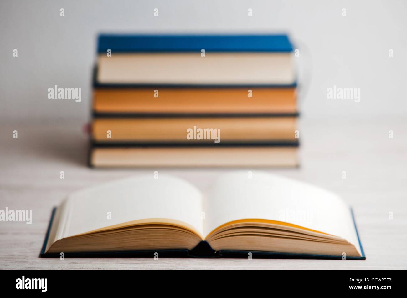 stack of books on wooden desk, with open book Stock Photo - Alamy