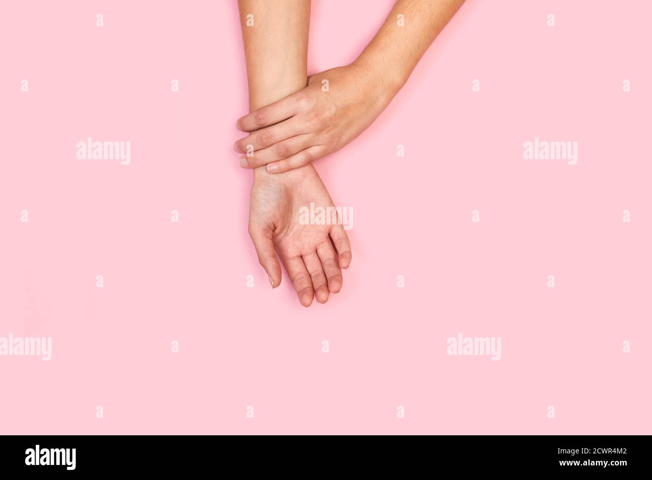 Woman hand touching her own wrist on a pink background in a top view ...