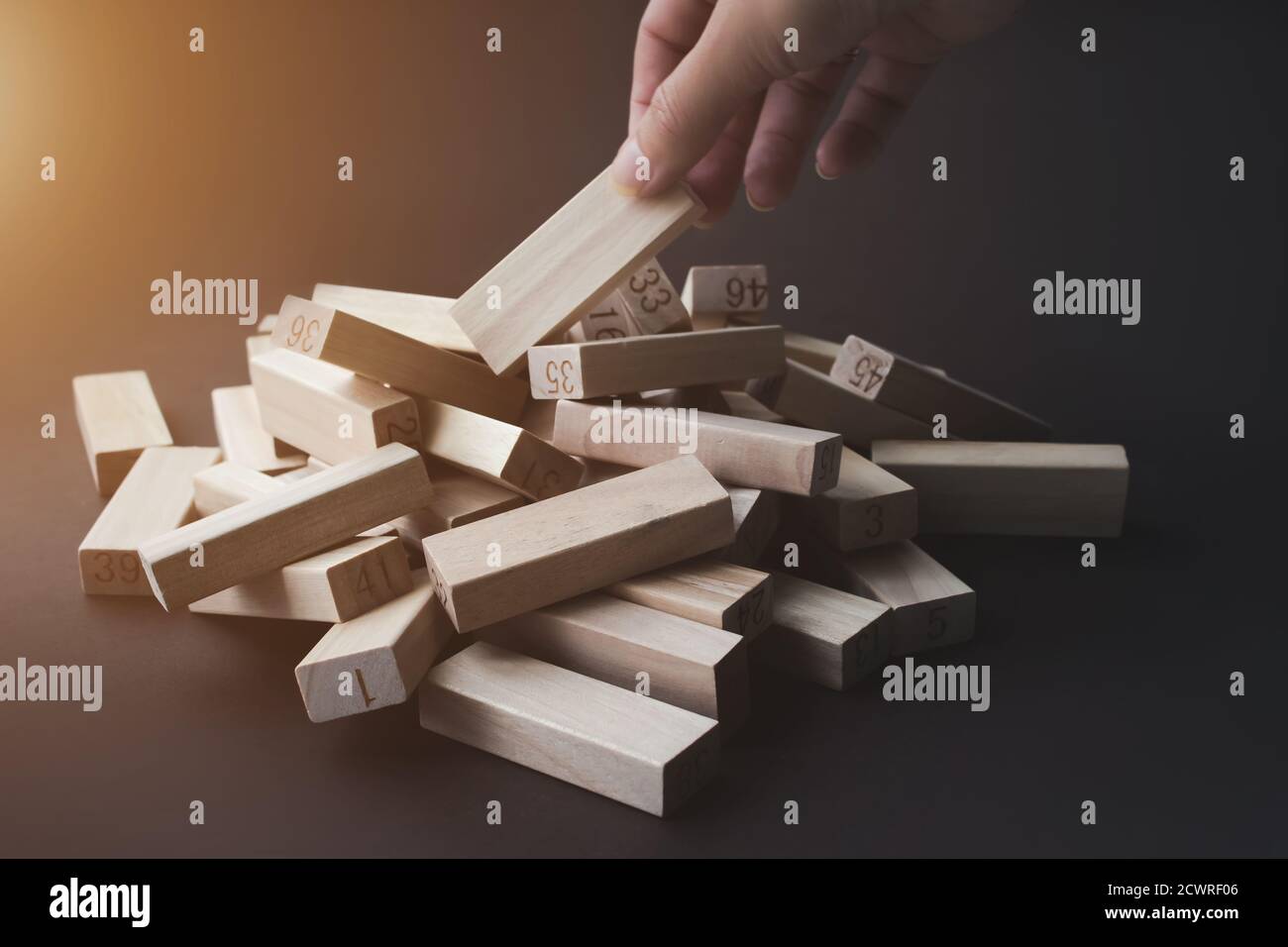 Hand pulls a wooden block from a pile of the same blocks on brown ...