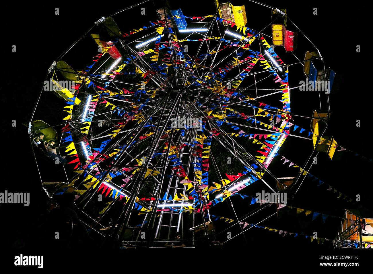Two lone passengers riding a colorful ferris wheel at night time at a ...