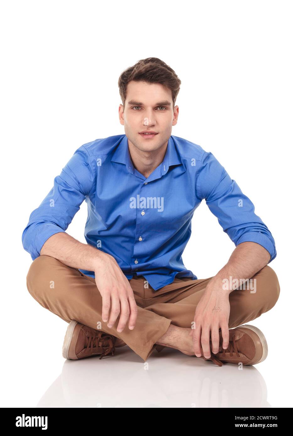 Handsome young man sitting with his legs crossed on isolated background ...