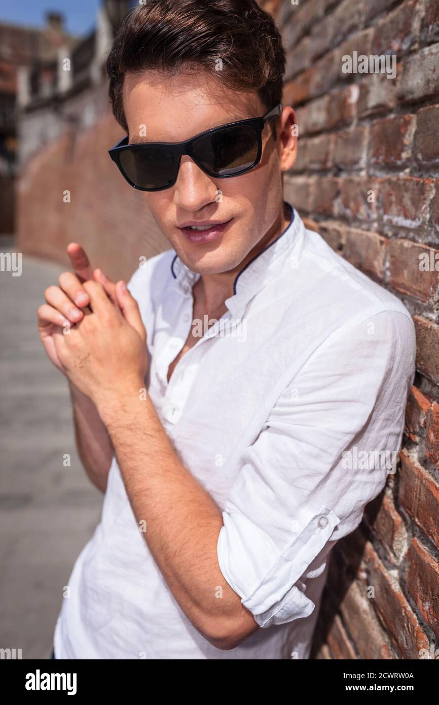 Side view of a young handsome man leaning on a brick wall while holding ...
