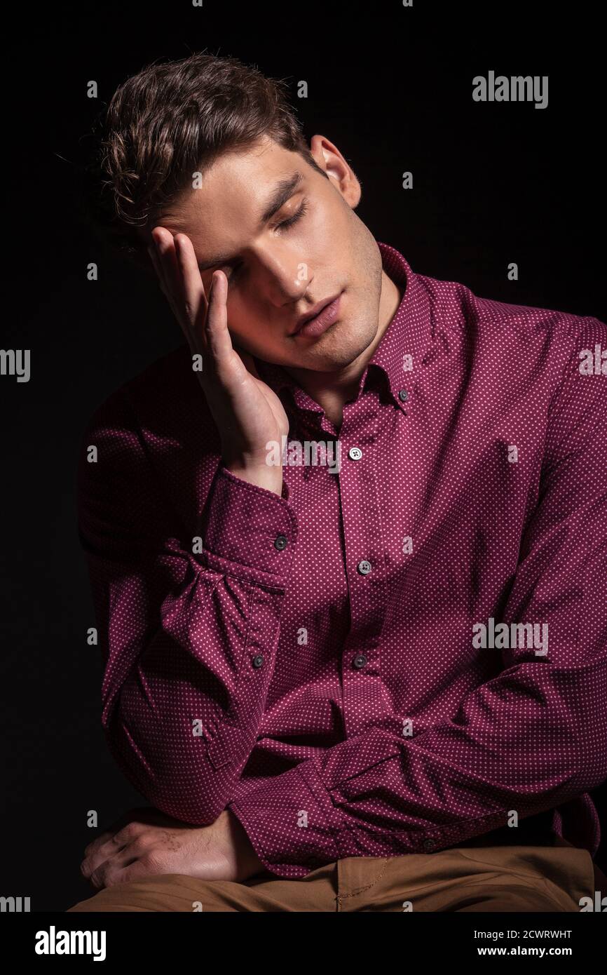 Young man leaning his head in his hand while holding his eyes closed ...