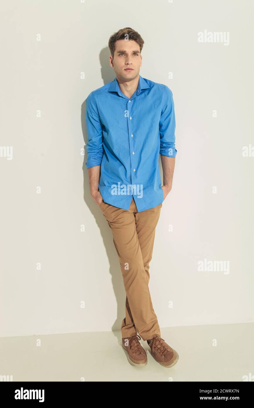 Casual young man leaning on a wall with his hands in pockets, holding ...